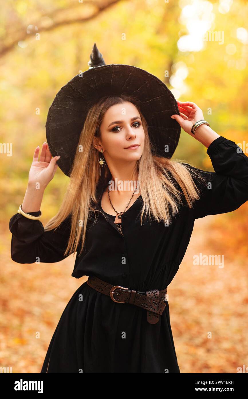 Blond woman in witch costume with broom walking on path covered with ...