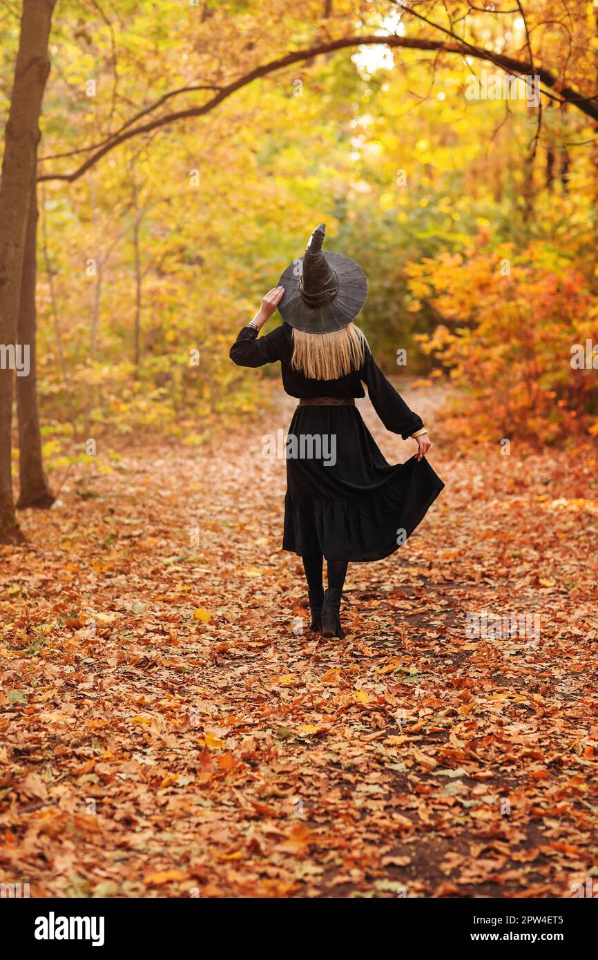 Back view of anonymous woman in witch costume with broom walking on ...
