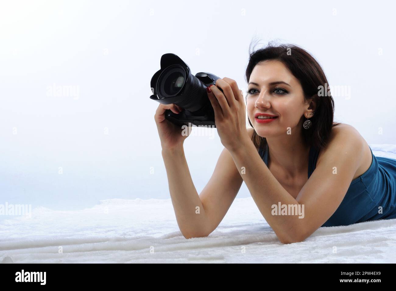 young woman l with a professional camera lying on the floor on white ...