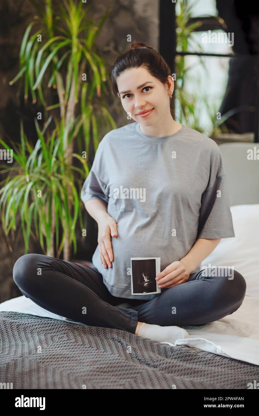 Pregnant woman holding pregnancy ultrasound while sitting in lotus pose ...