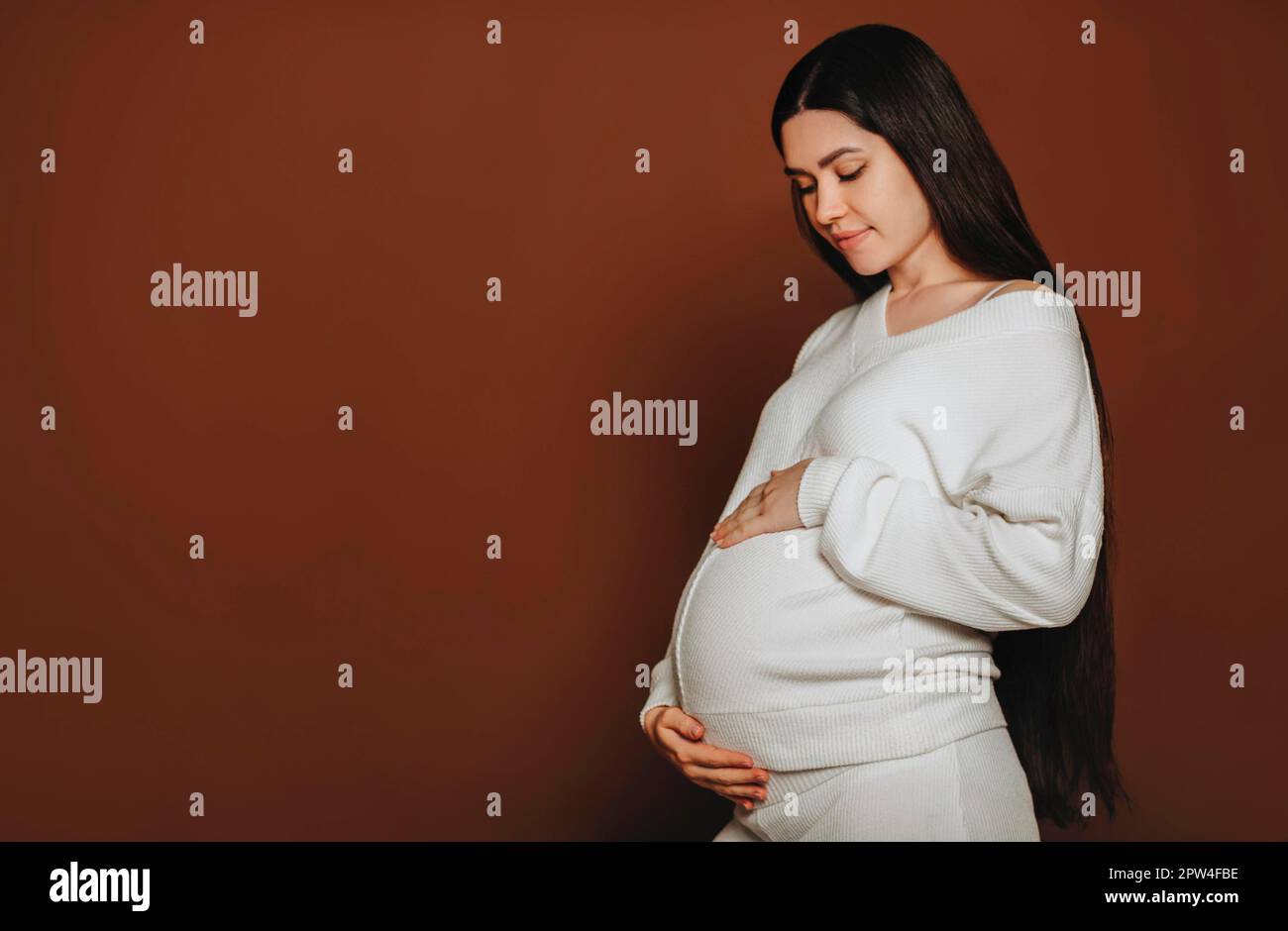 Young happy pregnant woman with long brown hair touching belly, talking ...