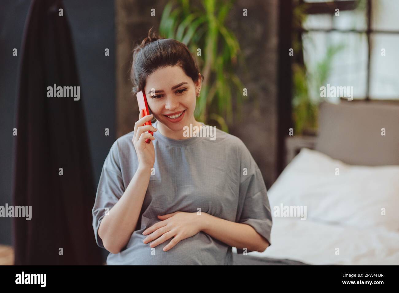 Young smiling pregnant woman touching belly talking on mobile phone ...