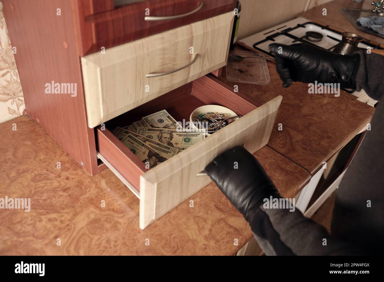 Robber in black outfit and gloves see in opened shelf in kitchen. The ...