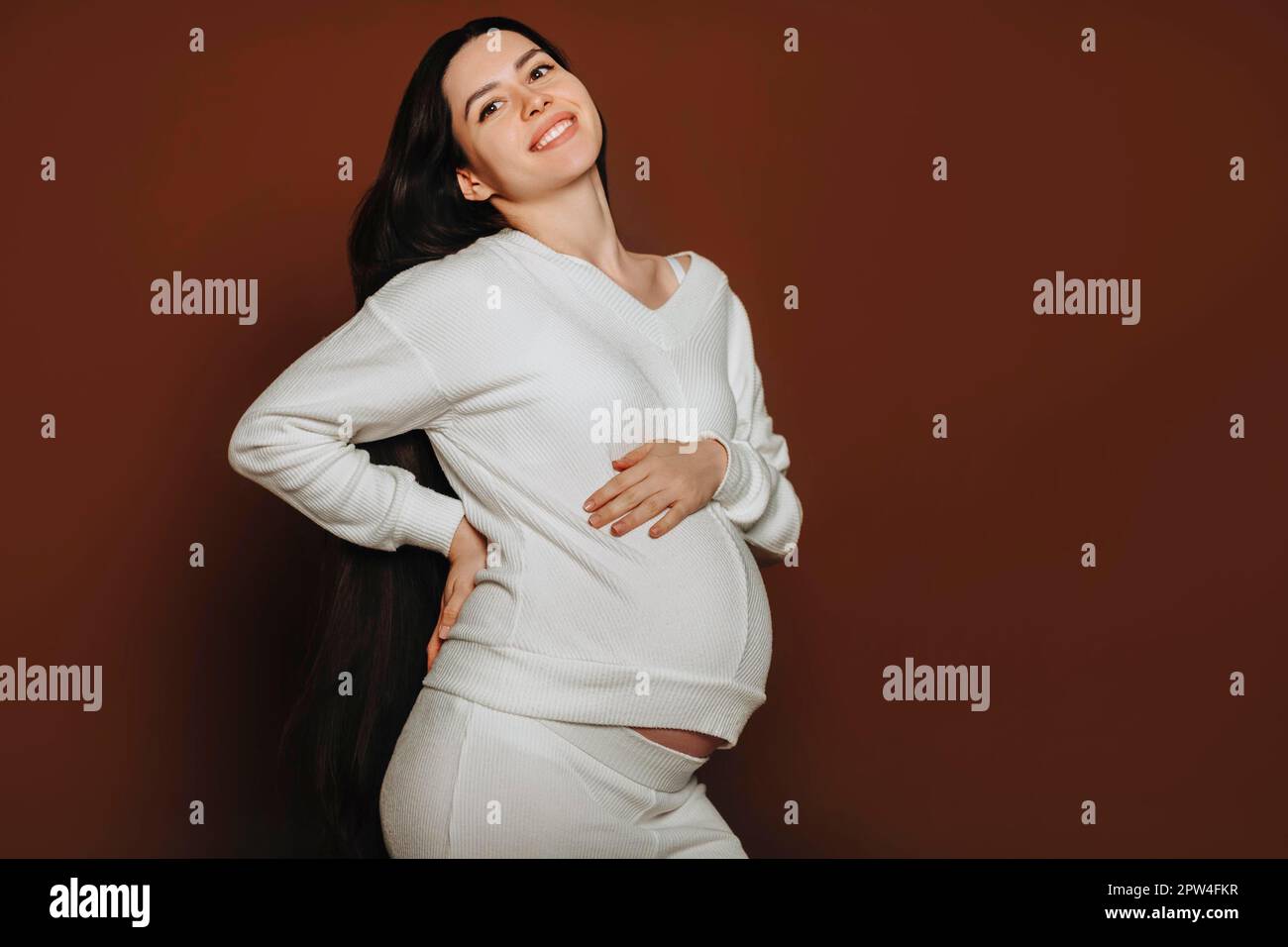 Young happy pregnant woman with long brown hair touching belly, talking ...