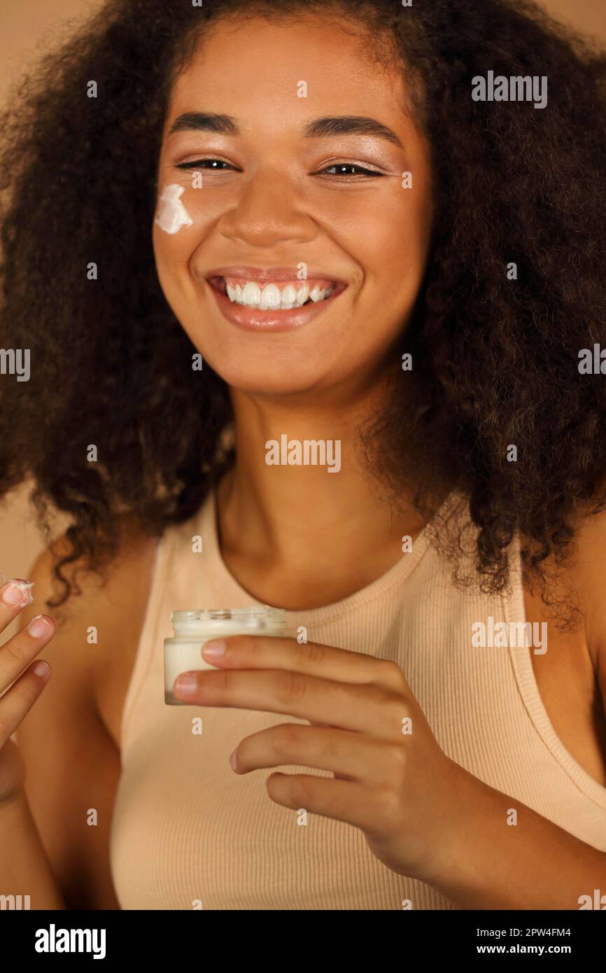 Smiling Dark Skinned Woman With Curly Afro Hair Applies Face Cream On