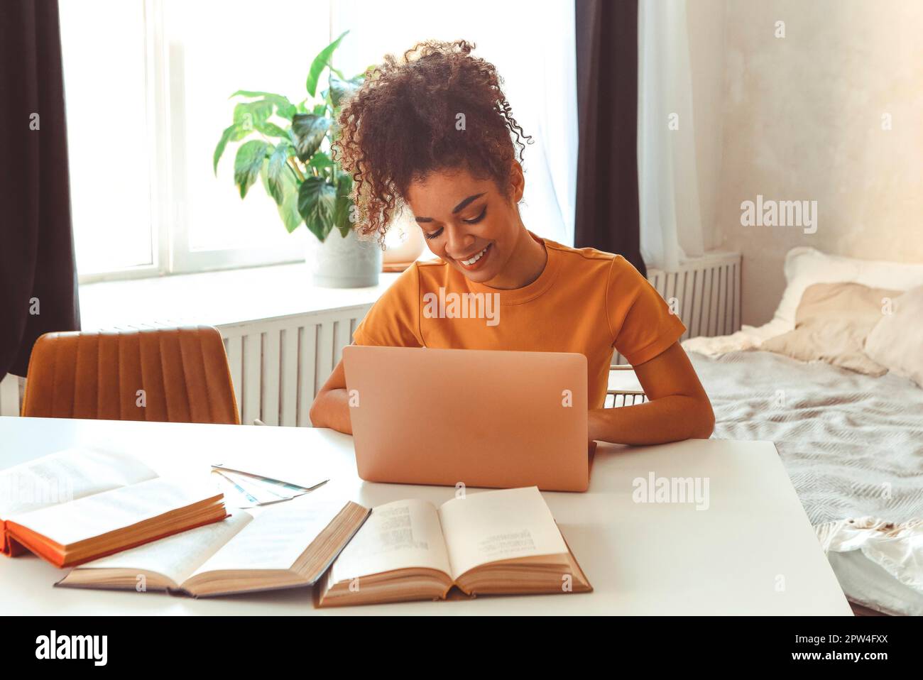 Cheerful young African American female student sitting at desk at home ...