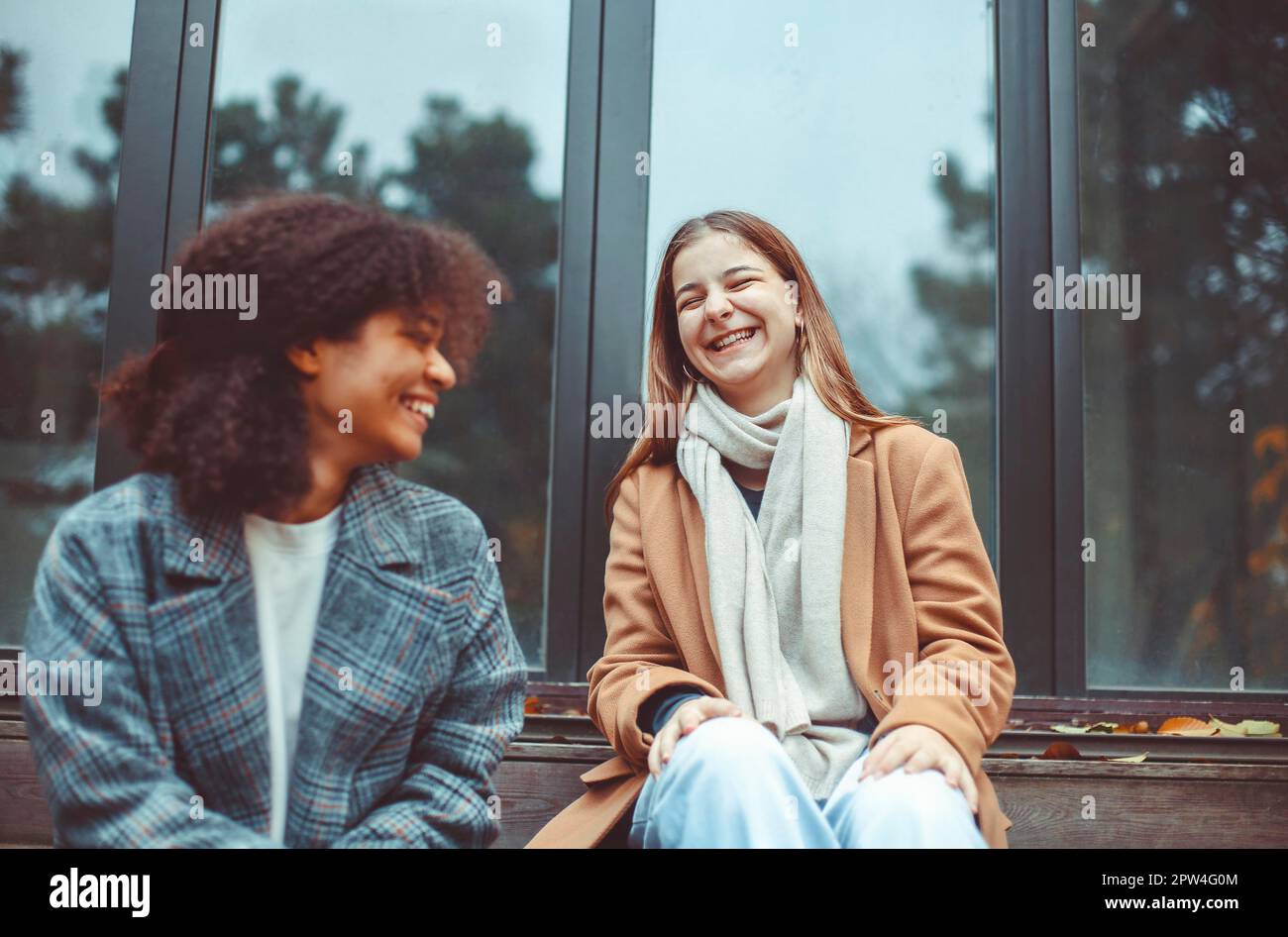 wo happy multiracial teen girls with takeaway coffee sitting outdoors ...