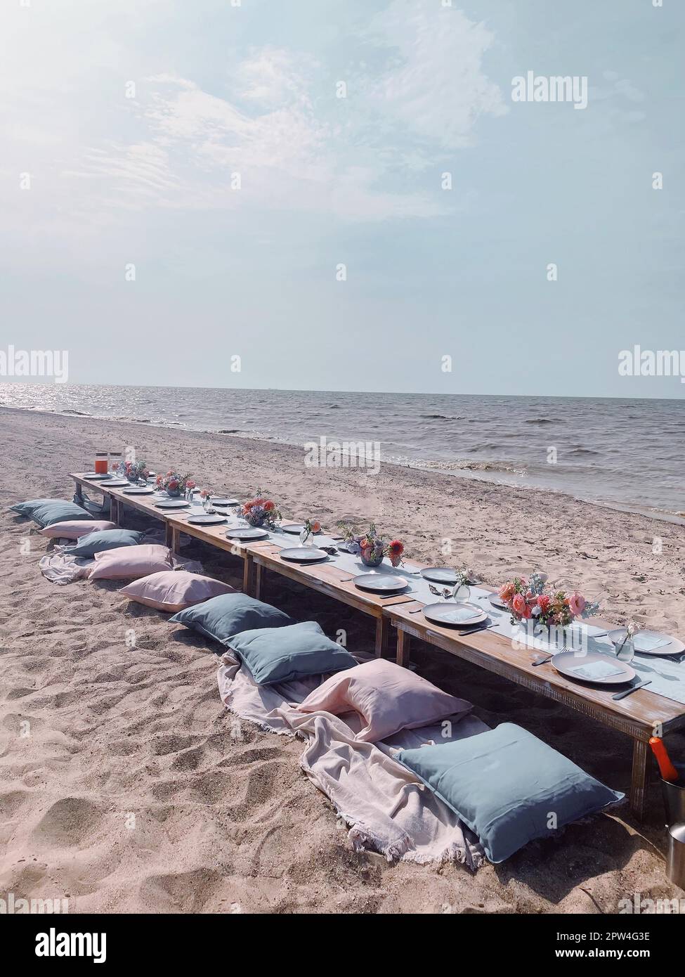 vertical photo of banquet table settings on beach with floral ...