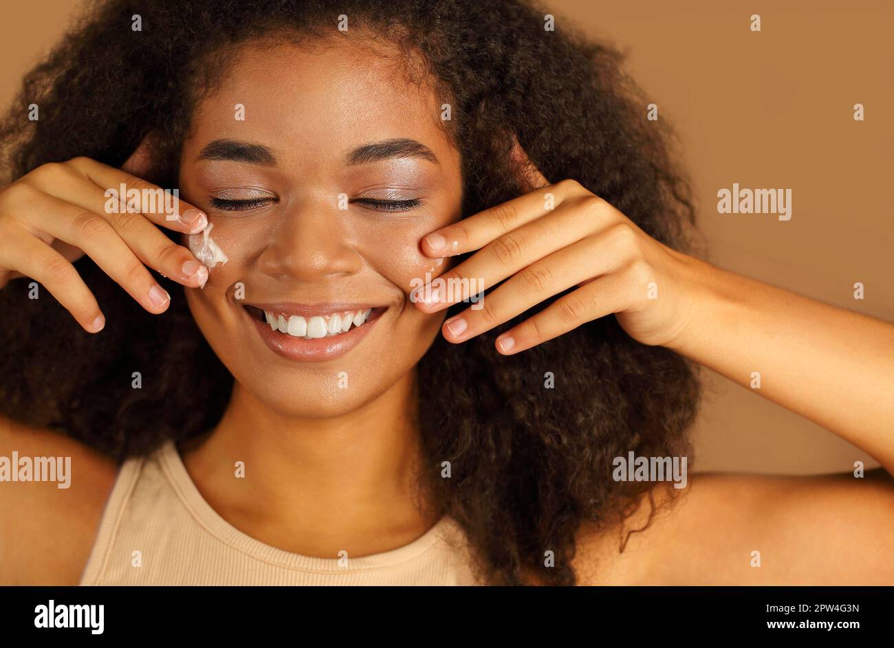 Smiling Dark Skinned Woman With Curly Afro Hair Applies Face Cream On
