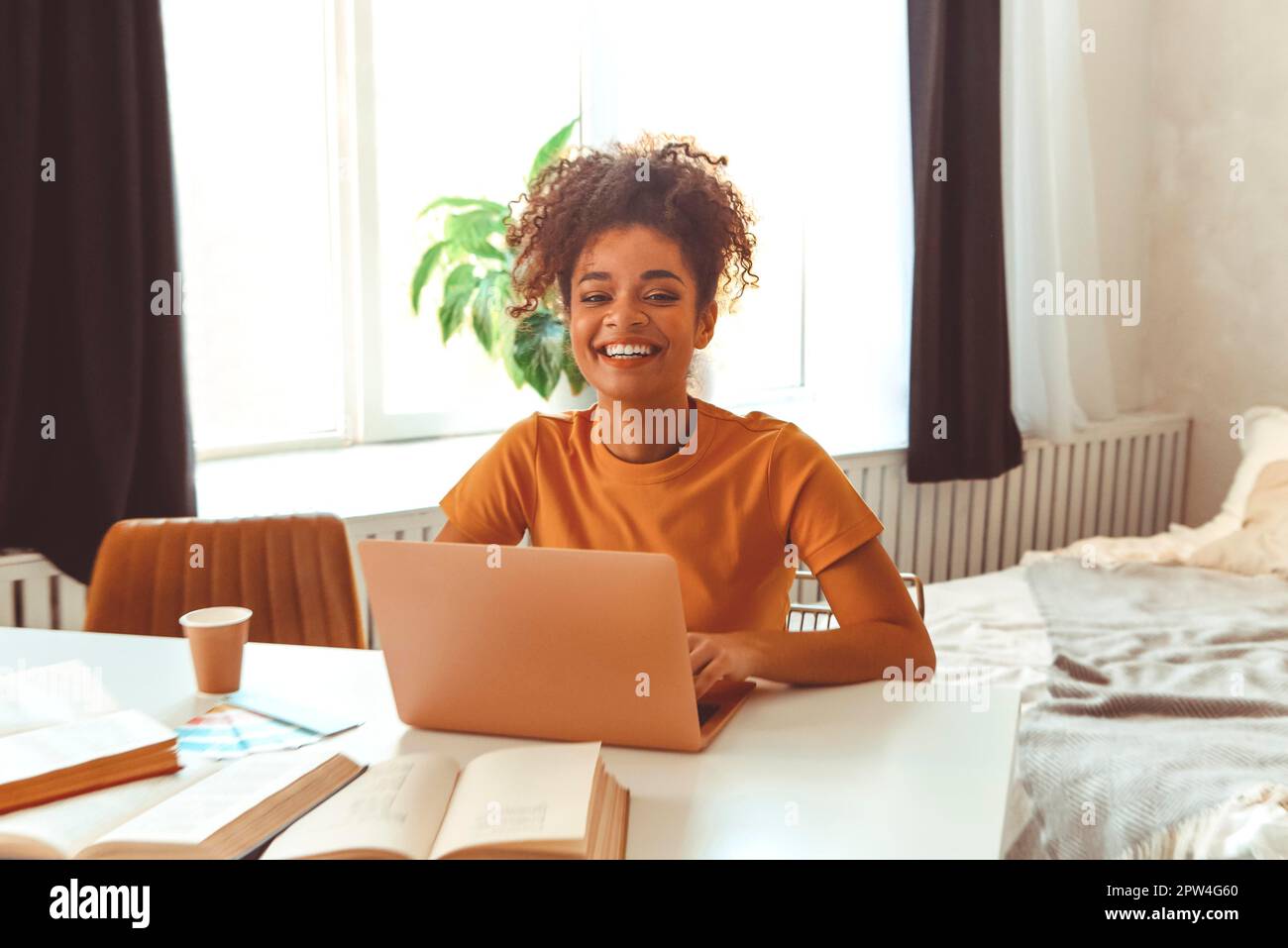 Cheerful young African American female student sitting at desk at home ...
