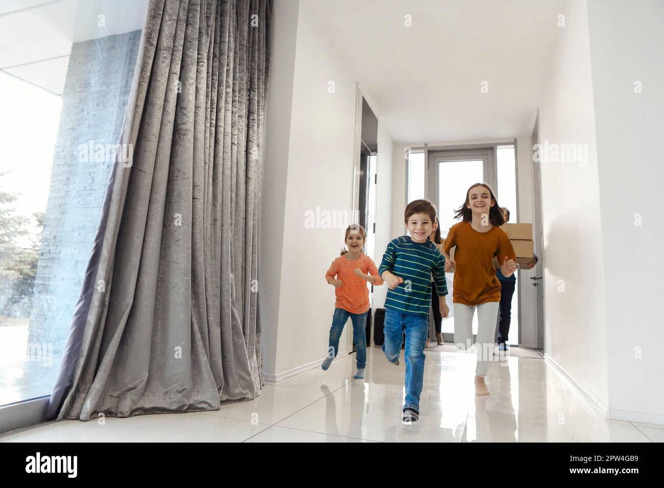Happy family running in hall. Funny kids jumping with carton box ...
