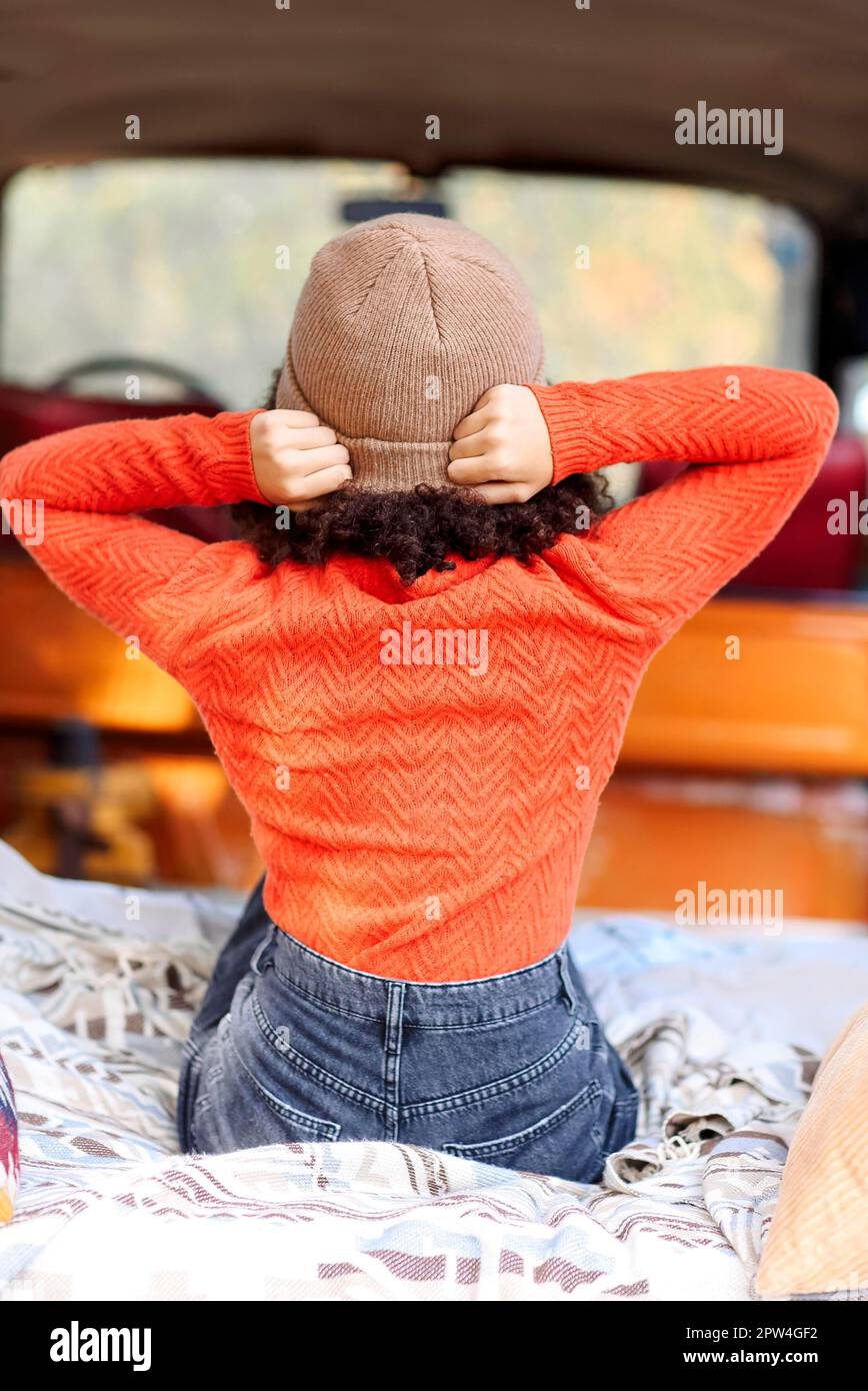 Rear view of young woman traveler sitting in minivan at campsite in ...