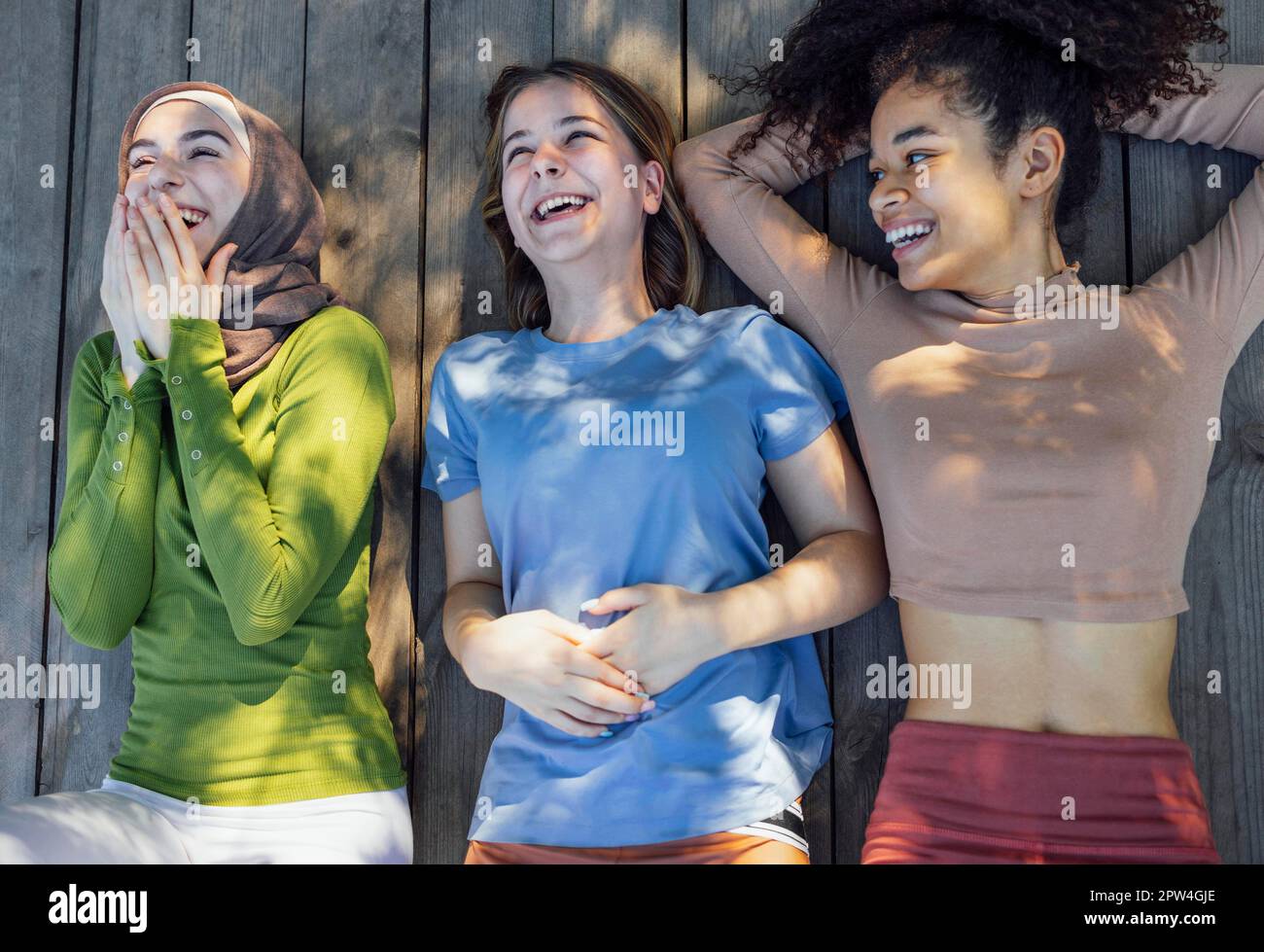 Multiracial young teen female friends resting in the park after sport training laughing and ...
