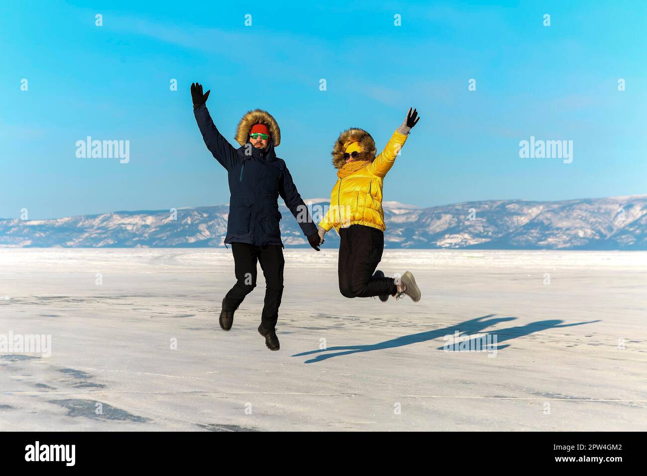 Happy couple is jumping on the frozen Lake Baikal. Transparent ice ...