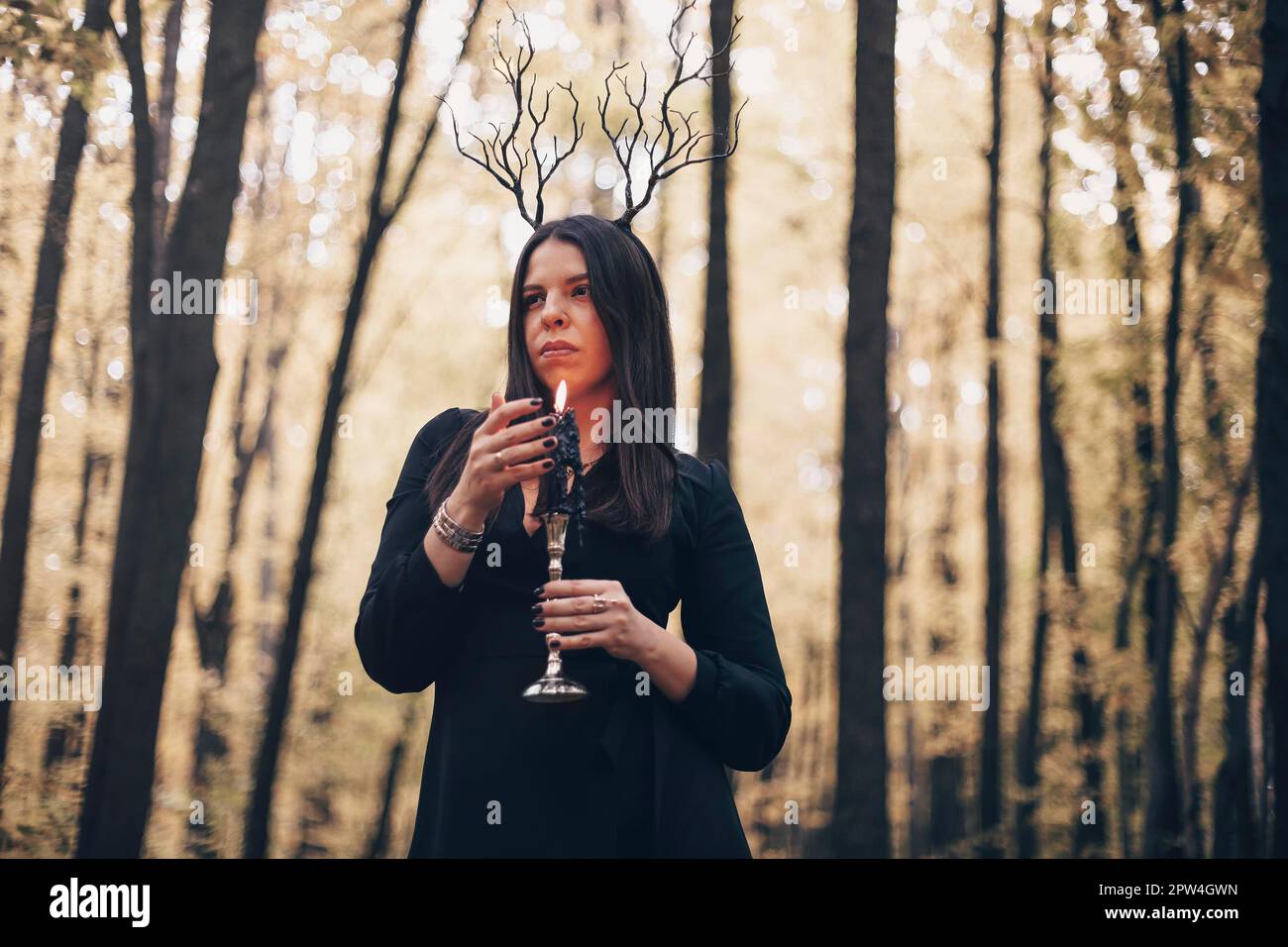 Shot of mysterious woman in black dress holding candle on candlestick ...