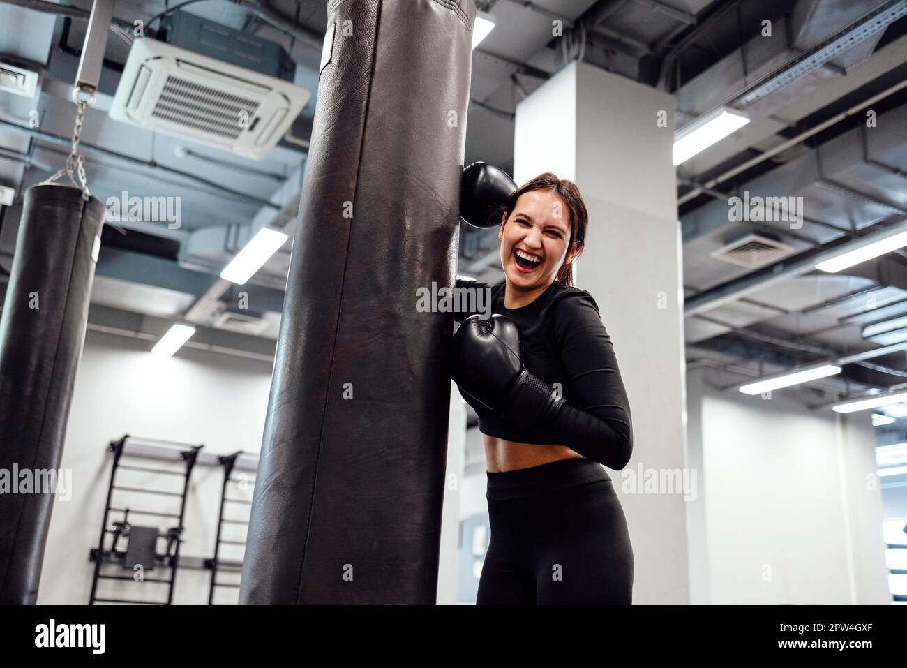 Strong latin boxing woman jump kick to huge punching bag at fitness gym ...