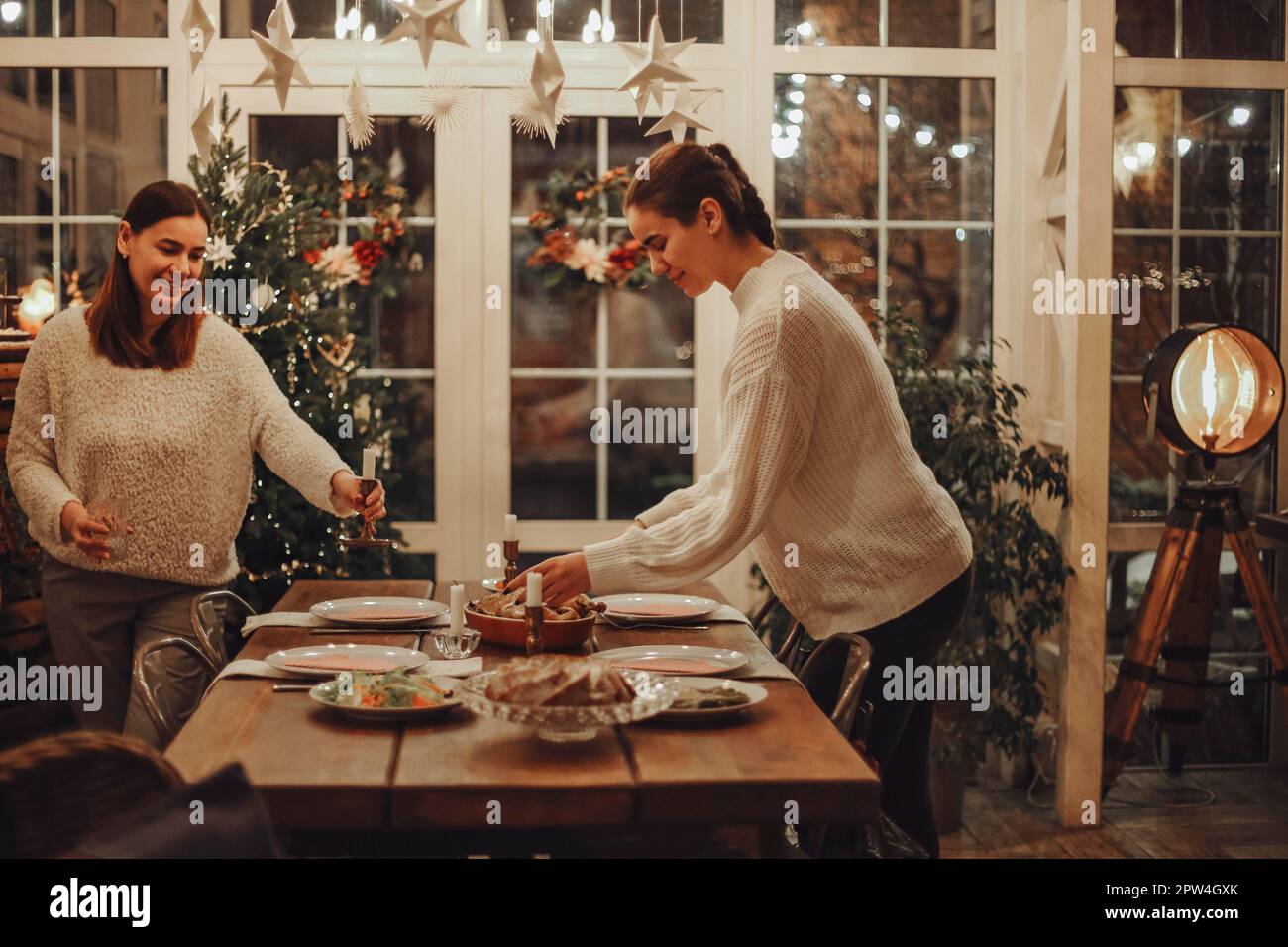 Two young women setting festive Christmas table together at home, happy ...