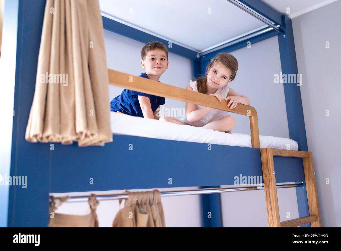 Caucasian little sibling are sitting on the bunk bed and looking to ...