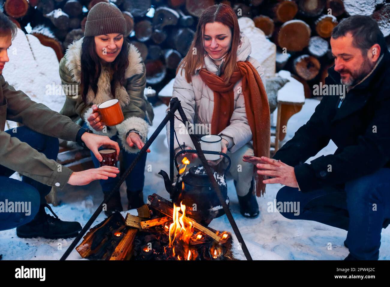 Group of friends gathering around bonfire in backyard, drinking tea and ...