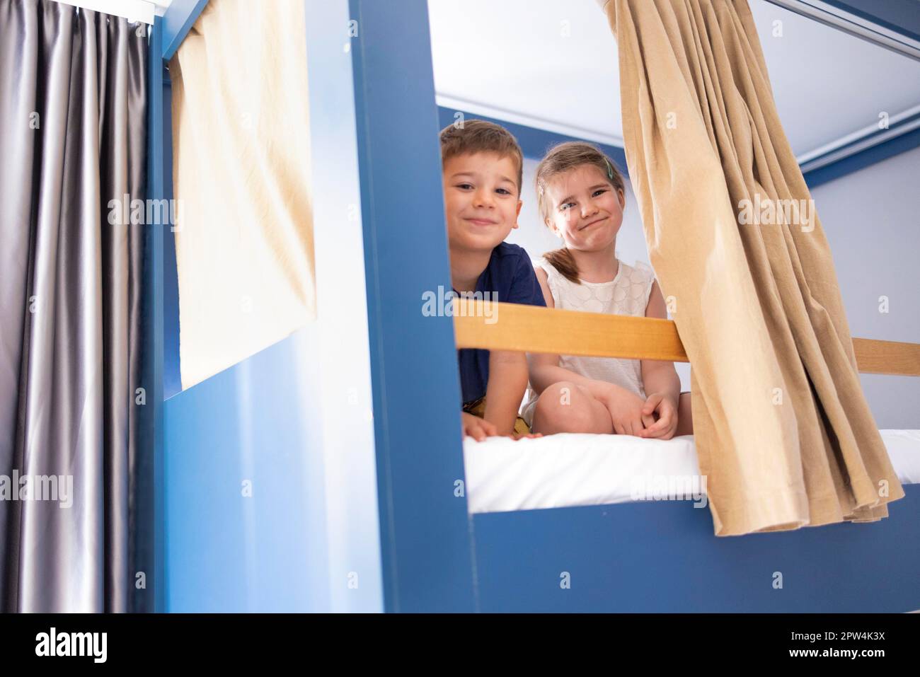 Caucasian little sibling are sitting on the bunk bed and looking to ...