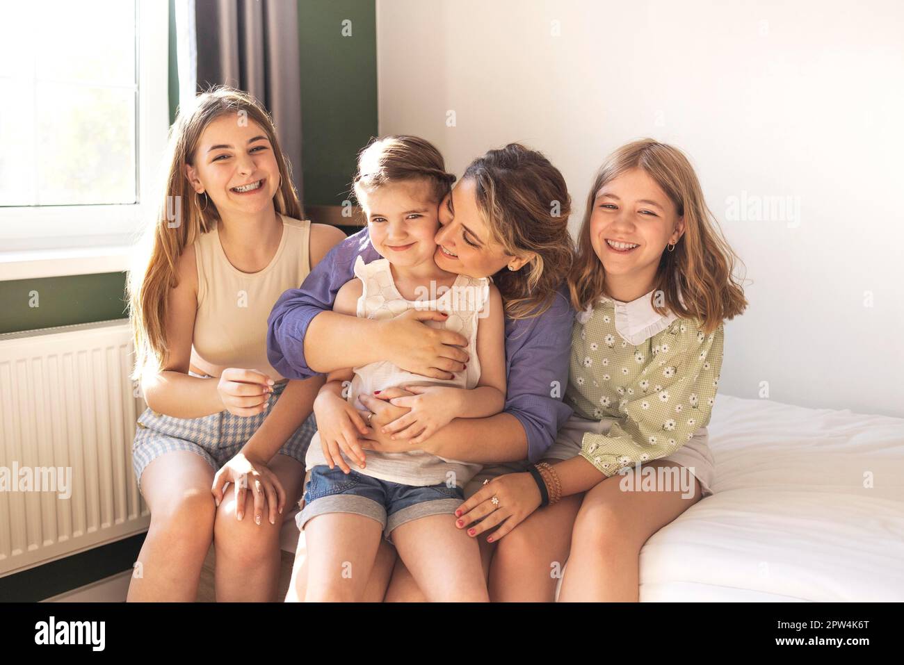 Happy three daughters and mother having fun enjoying conversations, sitting on sofa in modern ...