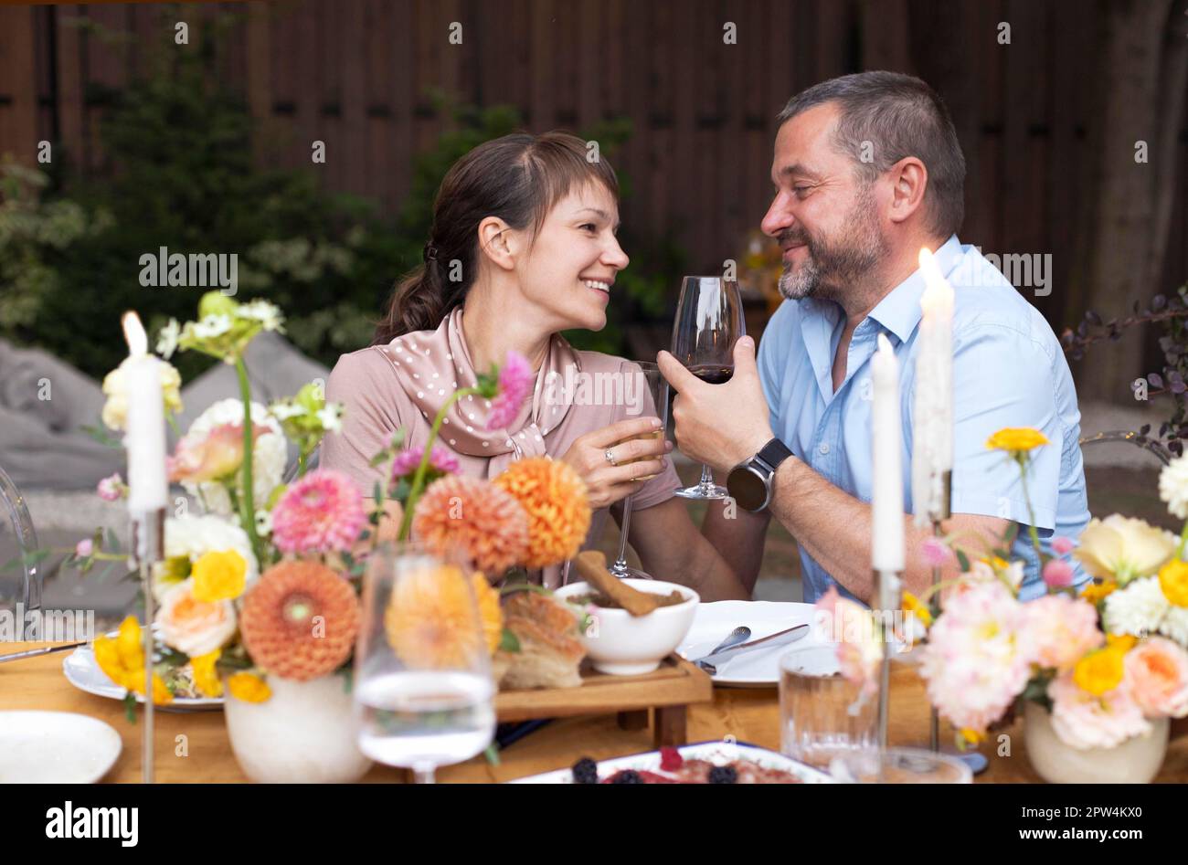 Happy couple talking and flirting in the terrace garden holding glasses ...