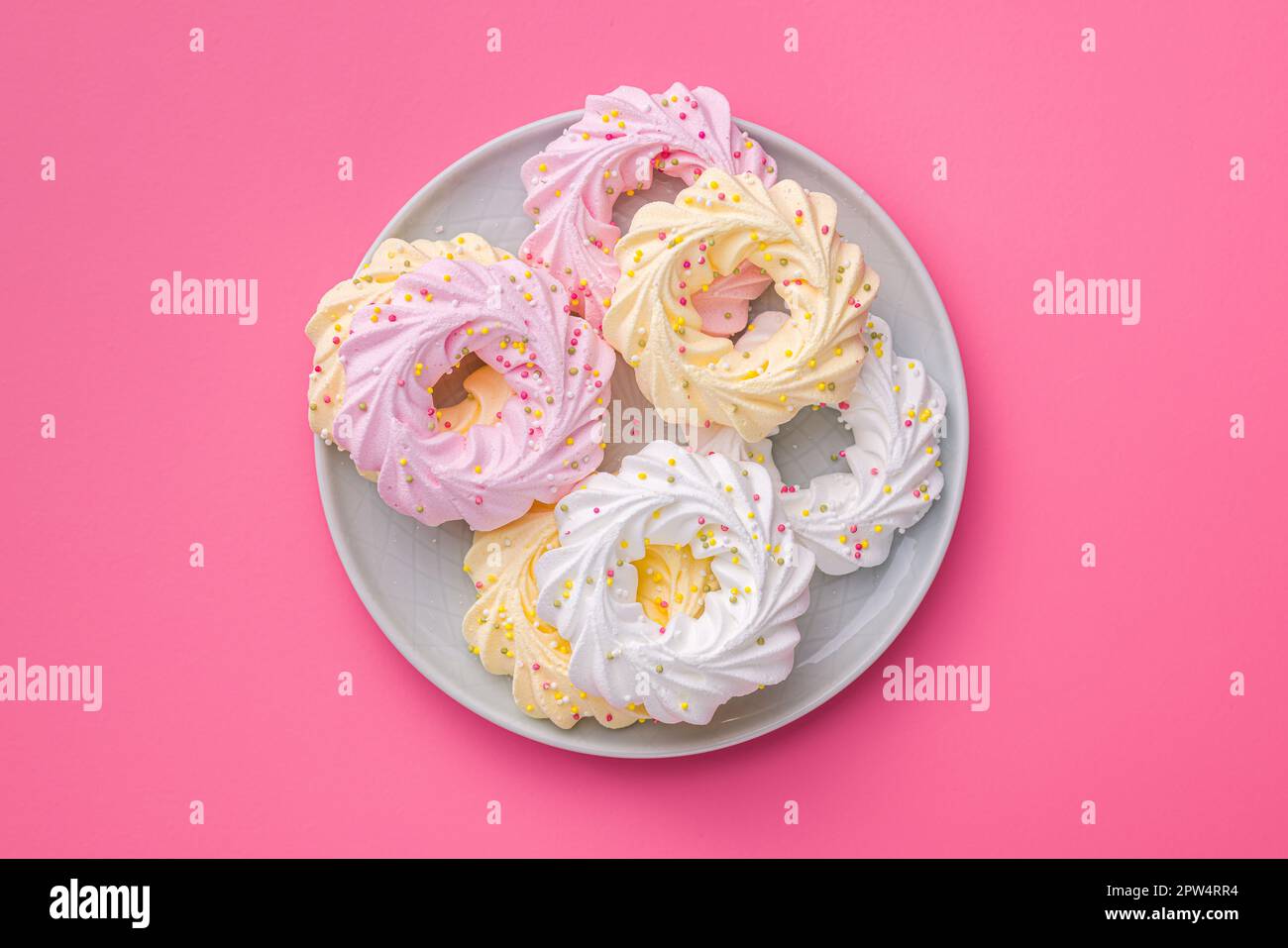 Different colors meringues with sprinkles on the plate on pink table ...