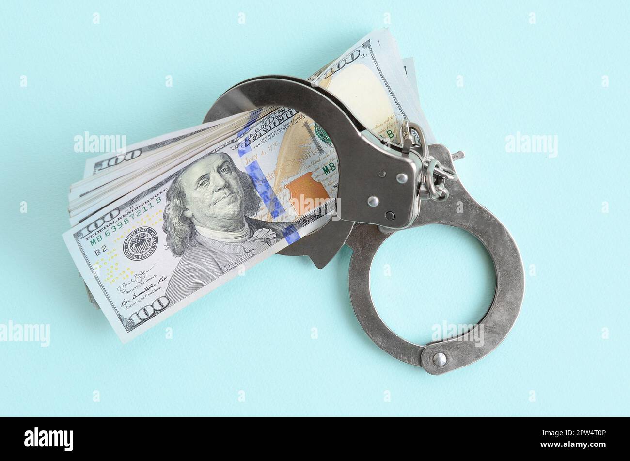 Silver police handcuffs and hundred dollar bills lies on light blue ...