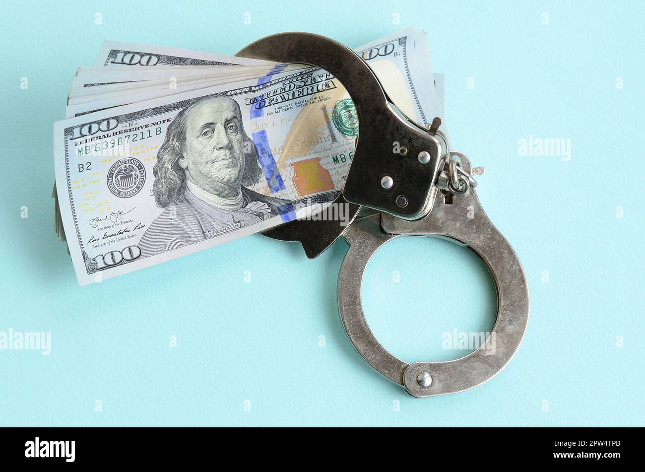 Silver police handcuffs and hundred dollar bills lies on light blue ...