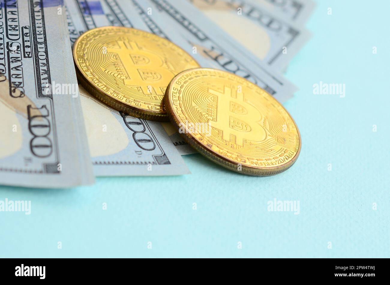 Golden bitcoins and hundred dollar bills lies on light blue background ...