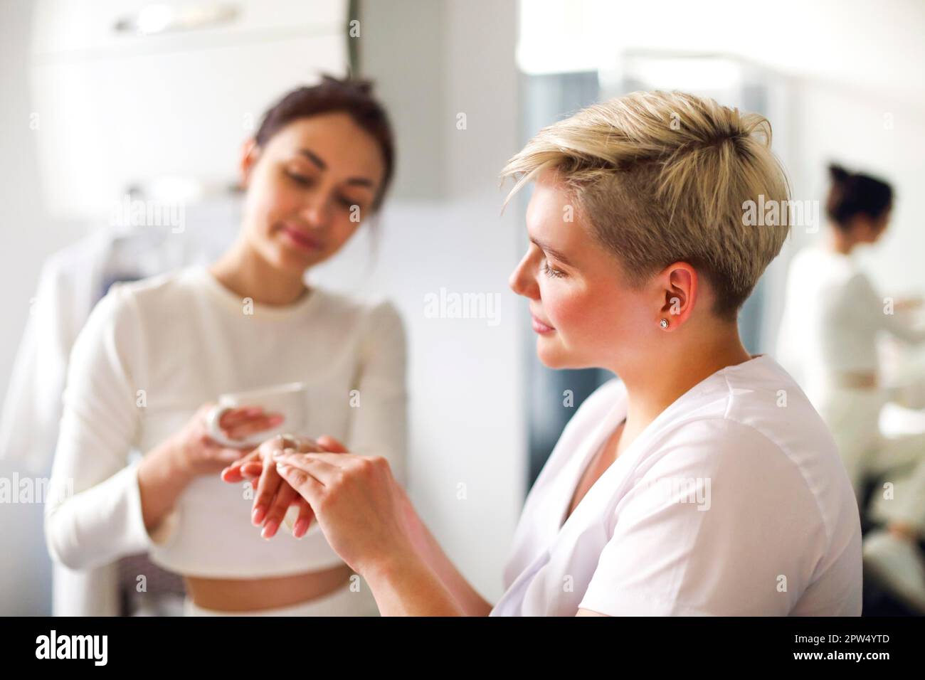 Female cosmetician applying moisturizing cream on hands of client ...