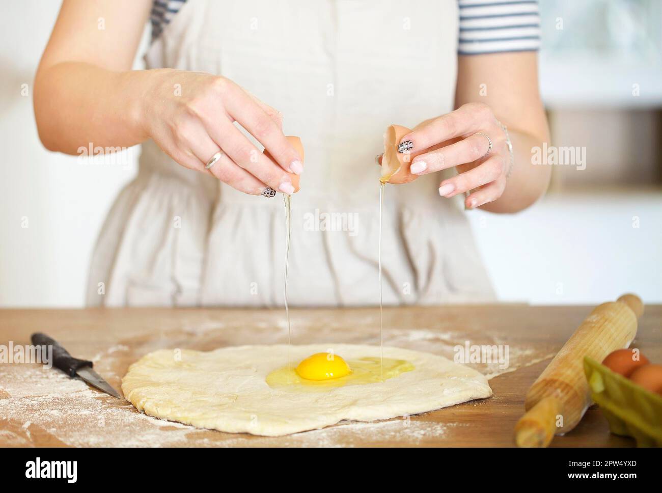 Unrecognizable housewife breaking egg over raw dough while cooking at table in kitchen Stock ...