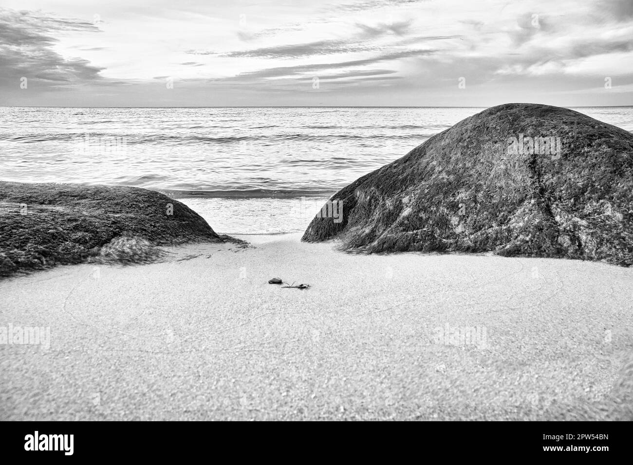 Big stone on the sandy beach in front of the sea with clouds in the sky ...