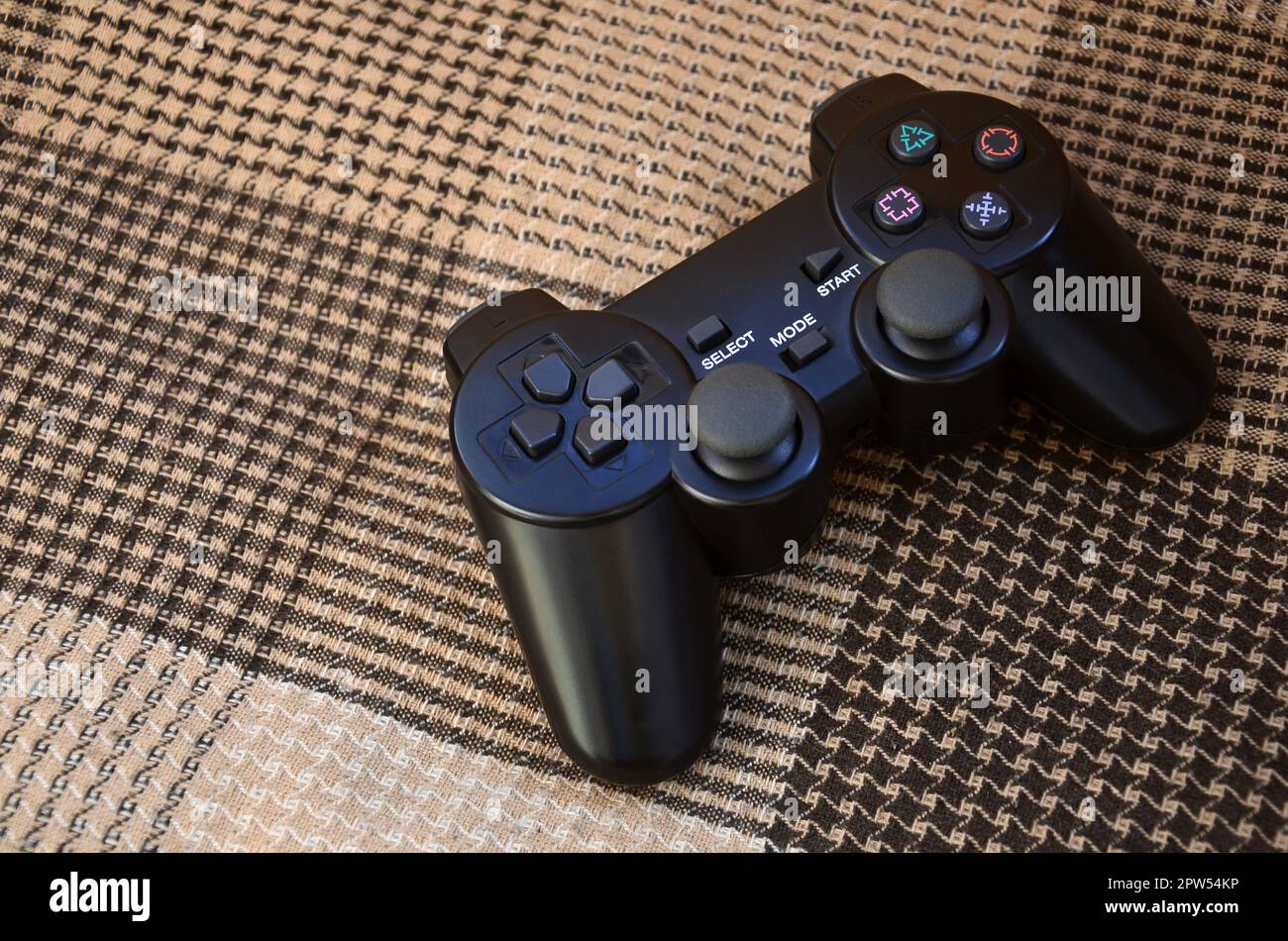 Modern black video game controller lies on a checkered beige and black ...