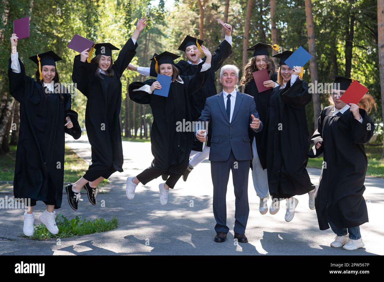 A university professor and seven robed graduates are jumping outdoors ...