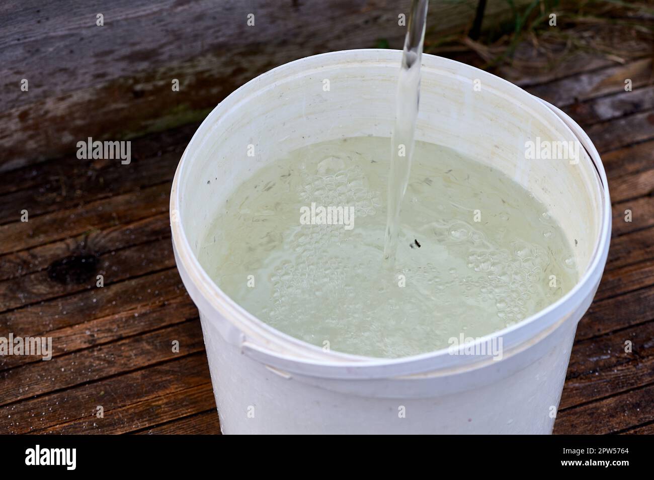 a white plastic bucket is filled with water from the pump. High quality ...