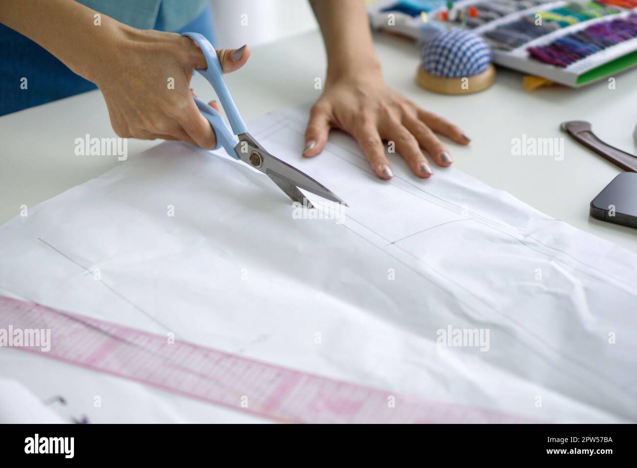 Closeup dressmaker hand use scissors to cut sketch paper pattern Stock ...