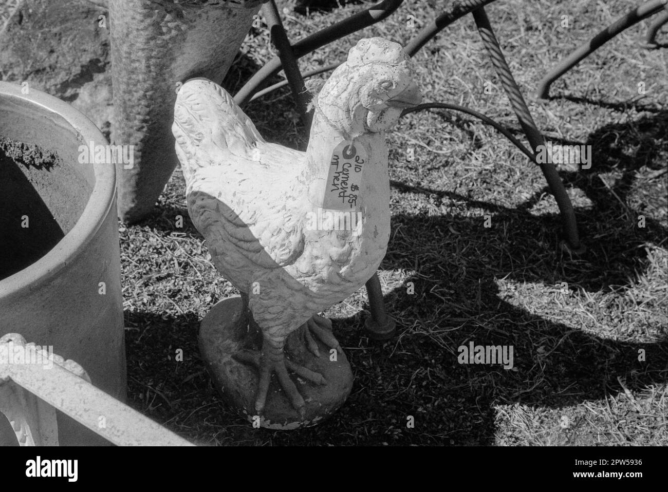 A white cement garden statue of a chicken on display at an antique sale ...