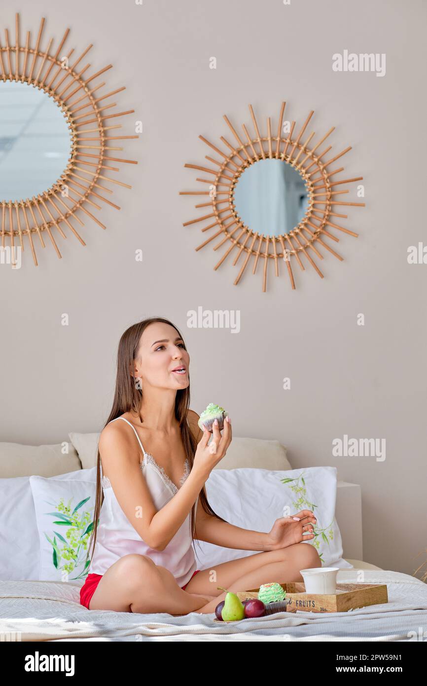 Beautiful girl biting cake while having breakfast in bed Stock Photo ...