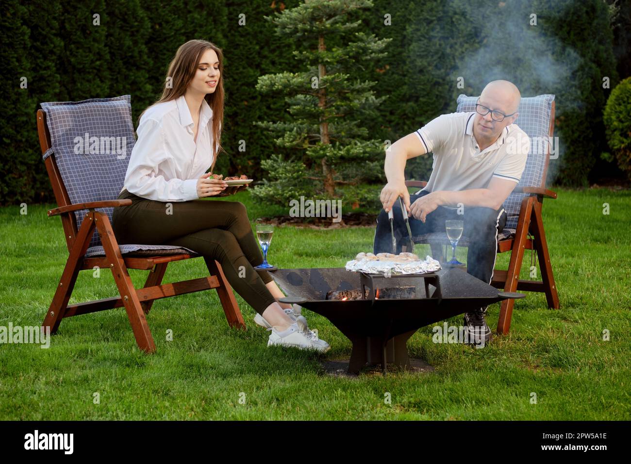 Happy couple barbecuing outdoors. Man turning sausages on grill Stock ...