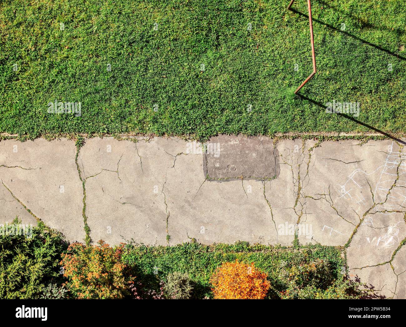 Old cracked pavement with green lawn and small bushes around. View from ...