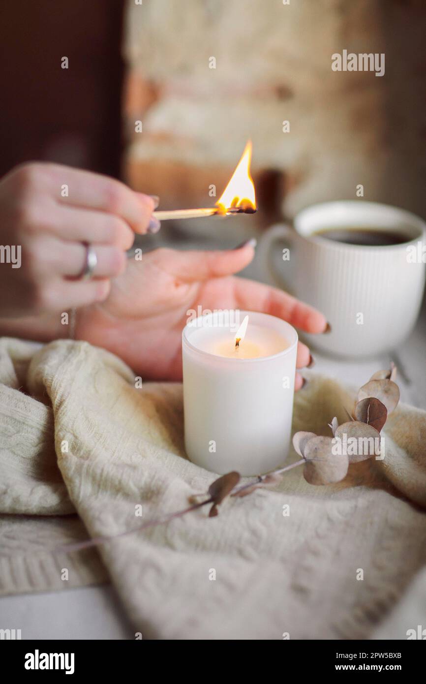 Female hands with lit match lighting burning candle on windowsill for ...