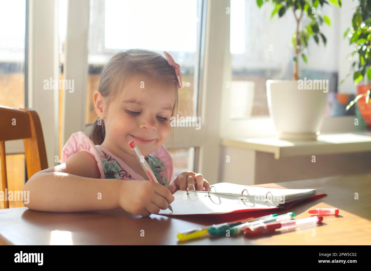 Adorable smiling little girl sitting at table and drawing with ...