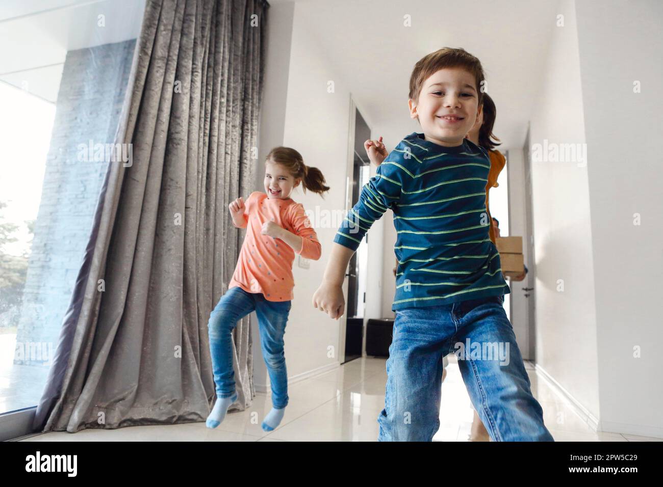Happy family running in hall. Funny kids jumping with carton box ...