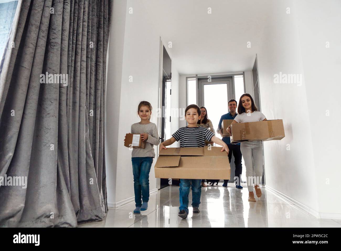 Happy family running in hall. Funny kids jumping with carton box ...