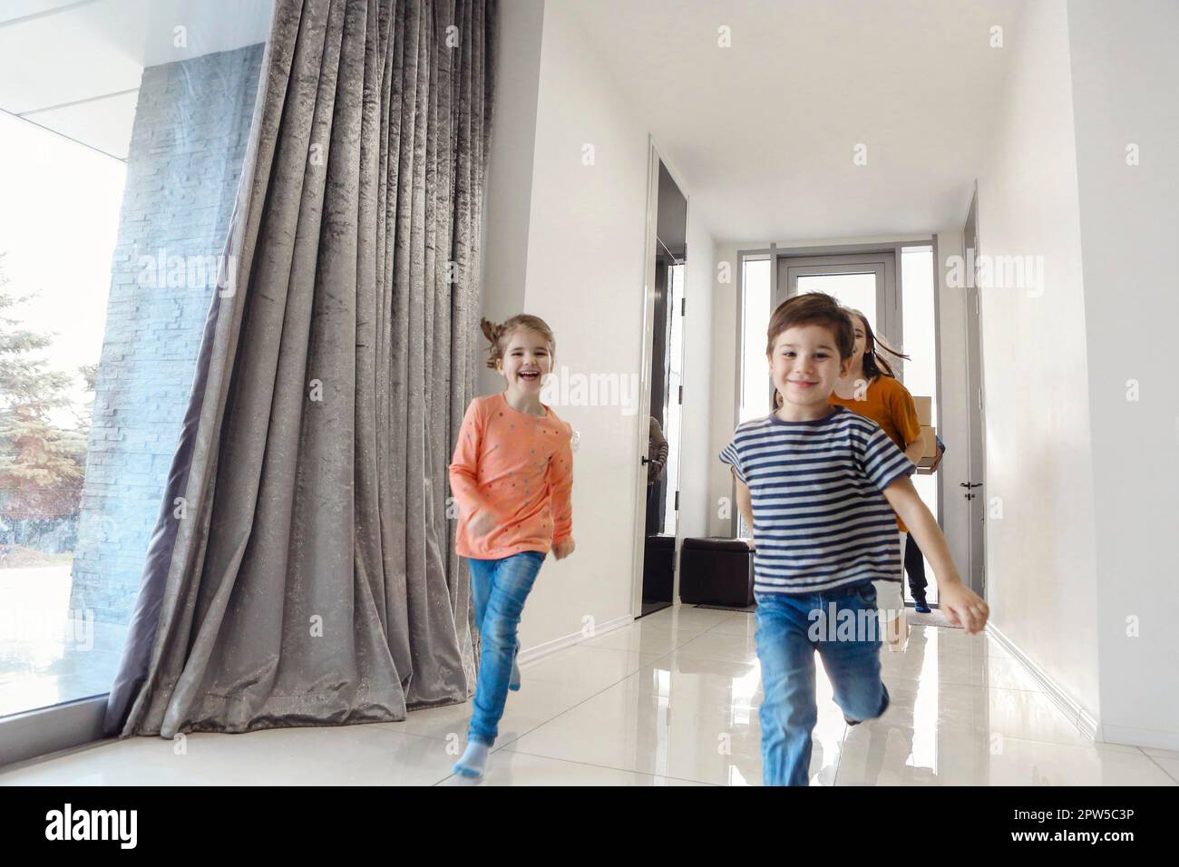 Happy family running in hall. Funny kids jumping with carton box ...