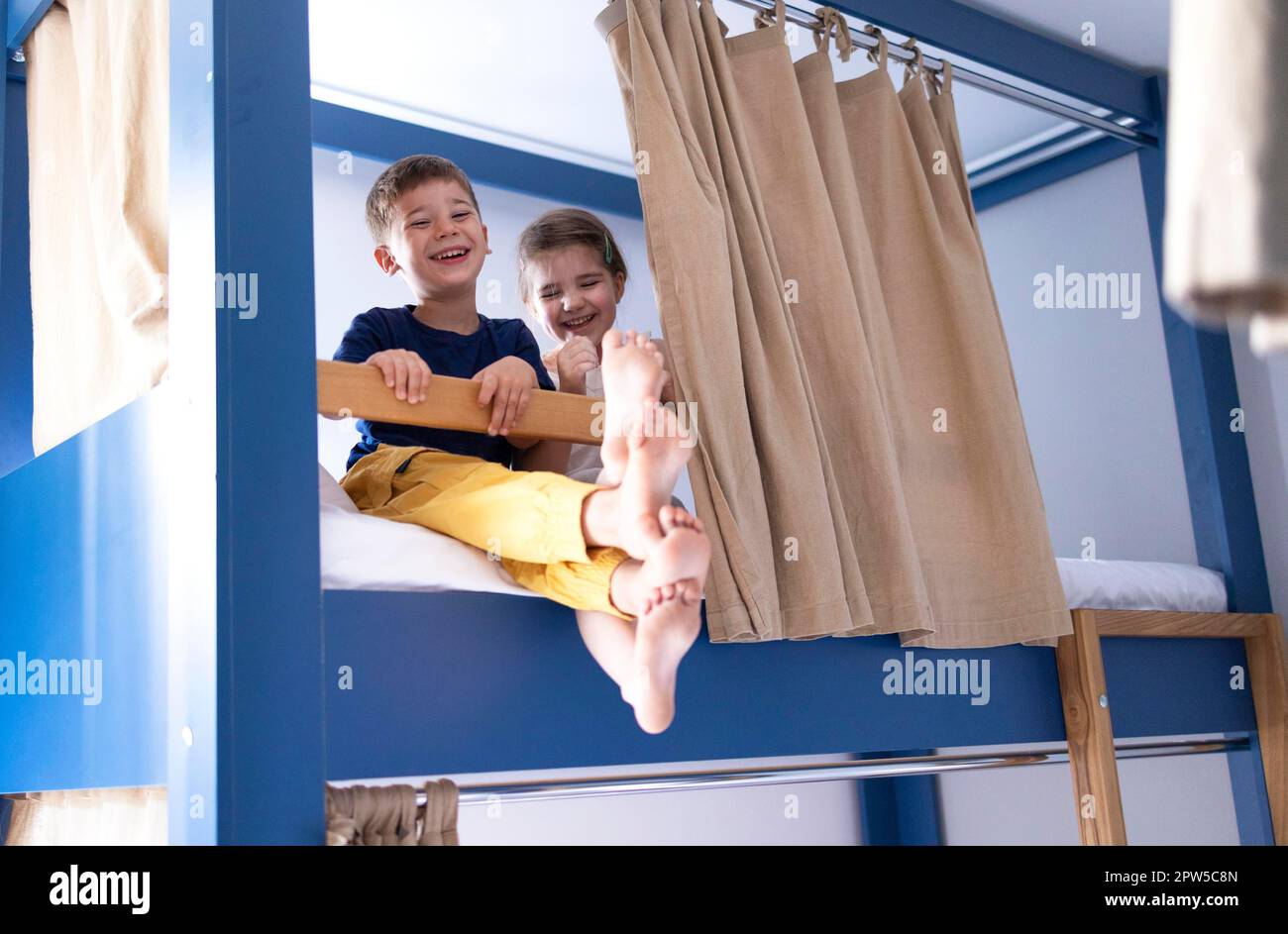 Caucasian little sibling are sitting on the bunk bed and looking to ...