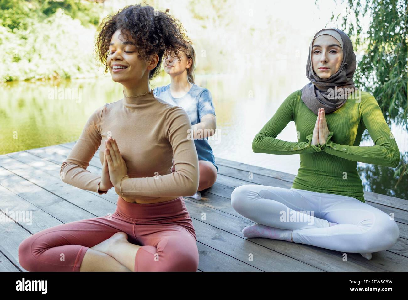 Group of teenages is engaged in fitness on pier by the lake or river ...