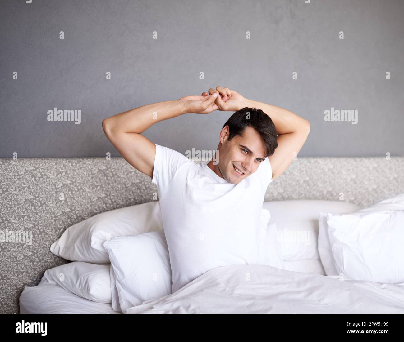 Well rested. a young man stretching in bed while waking up Stock Photo - Alamy