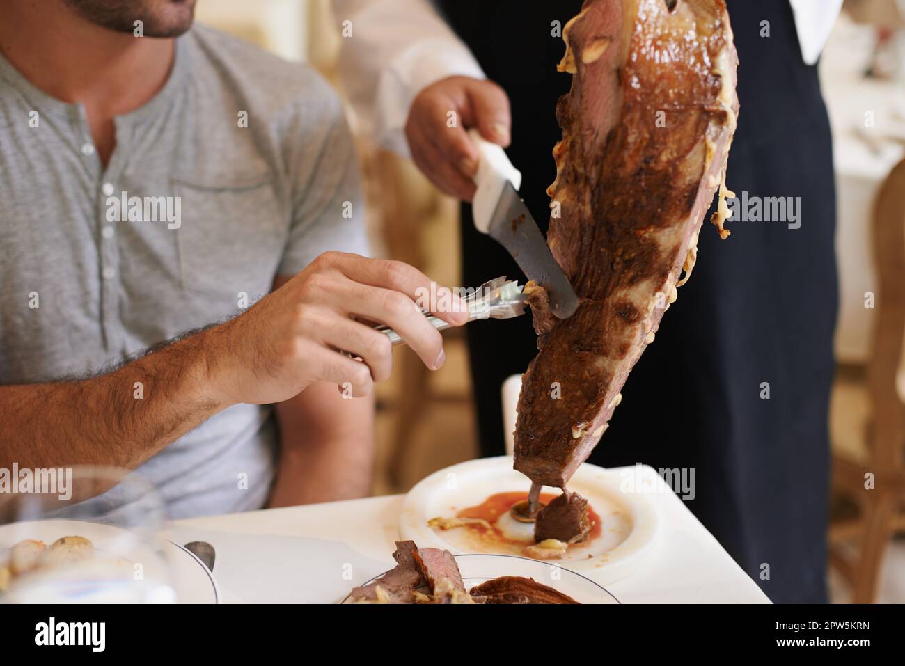 Men love their meat. A waiter cutting meat off a skewer at a diners ...